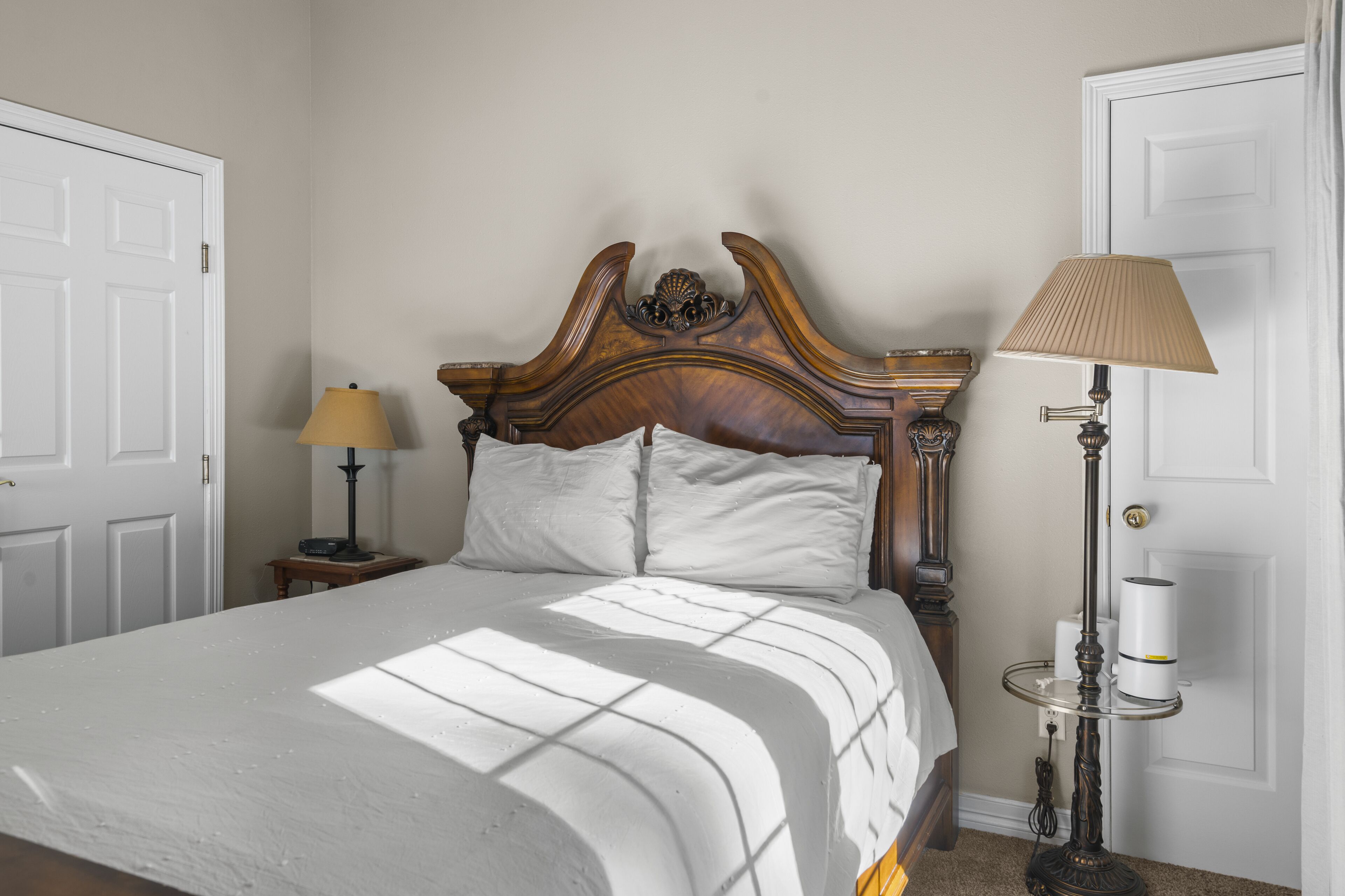 Cama bem arrumada com cabeceira de madeira, abajur, mesa de cabeceira com luminária e caixa de lenços.