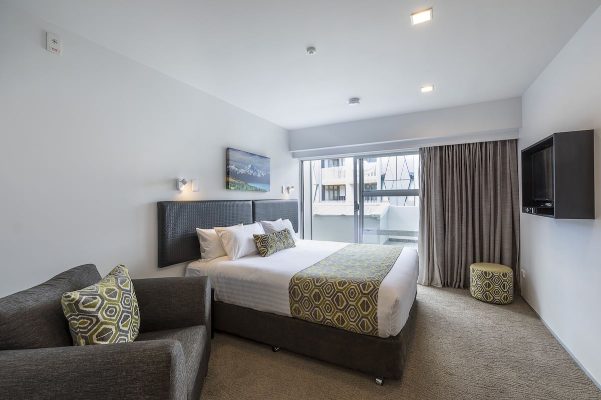 Quarto de hotel moderno com cama grande, sofá, televisão e vista para o exterior.
