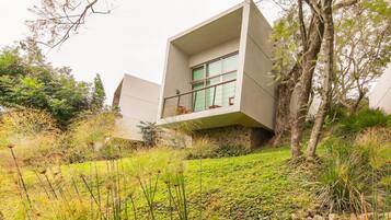 Uma casa moderna com uma varanda em balanço e paisagem exuberante de vegetação e árvores.