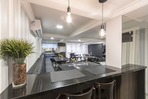 Uma cozinha moderna com bancada preta, banquetas e uma área de estar com mesas e cadeiras.