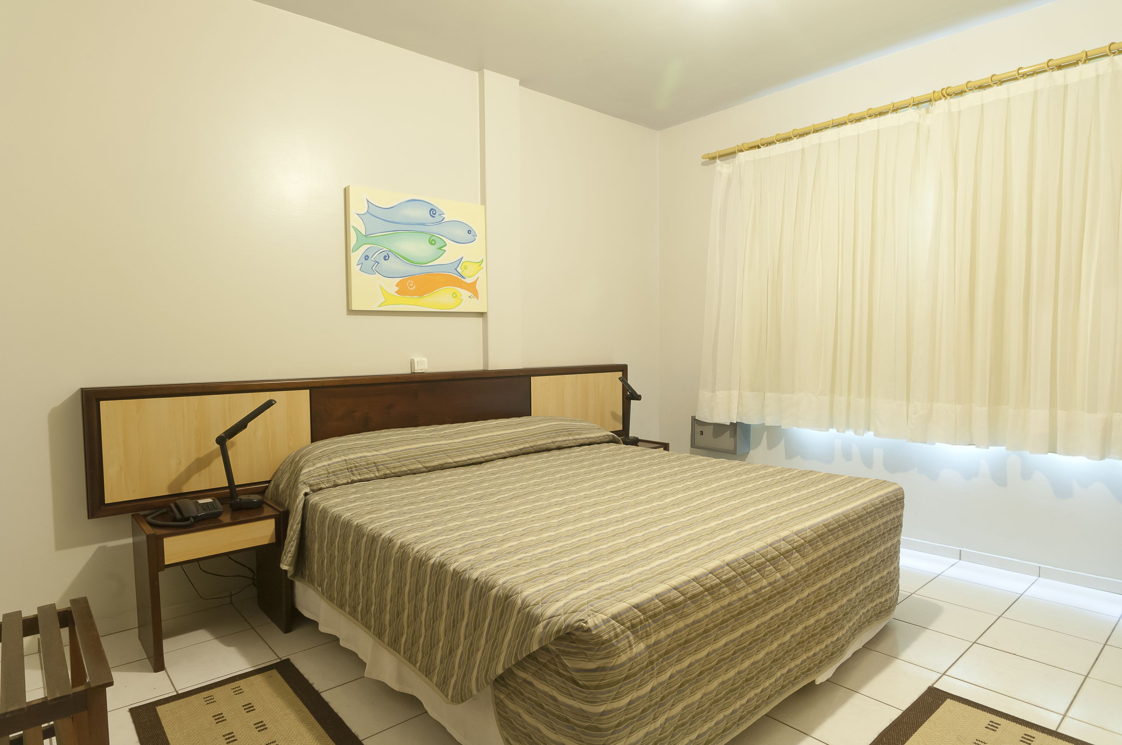 Quarto com cama, mesa de cabeceira, abajur e um quadro na parede.