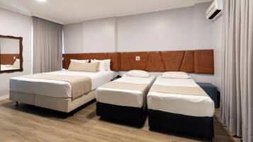 Quarto de hotel com três camas, cabeceira de madeira, espelho e ar condicionado.