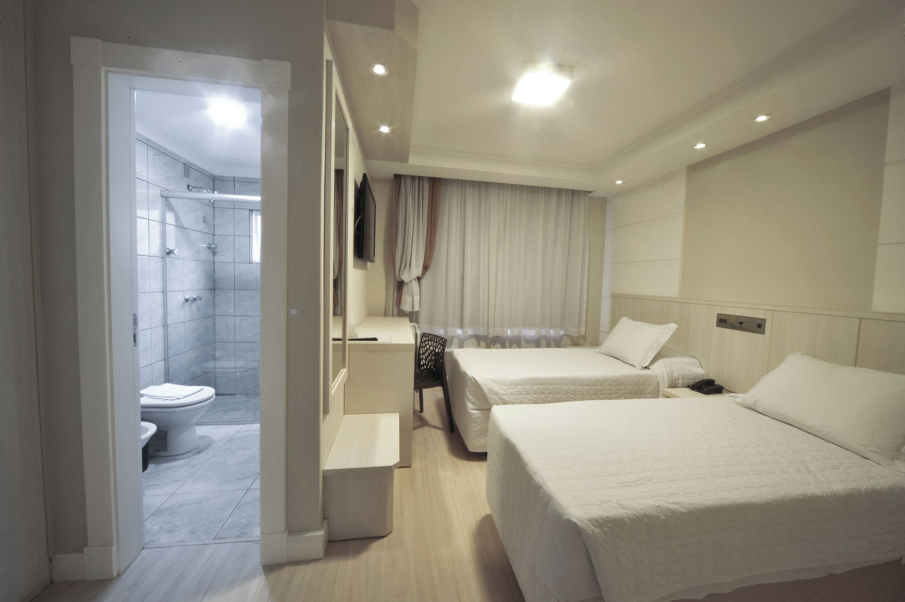 Quarto de hotel com duas camas, banheiro com chuveiro e vaso sanitário.