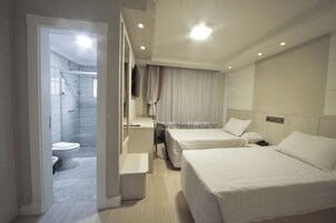 Quarto de hotel com duas camas, banheiro com chuveiro e vaso sanitário.