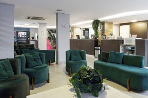 Um lobby moderno com sofás verdes, uma máquina de café e uma mesa de recepção.