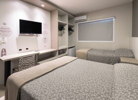 Quarto de hotel com duas camas, uma escrivaninha, televisão e guarda-roupa.