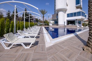 Uma área à beira da piscina com espreguiçadeiras e um edifício moderno ao fundo.