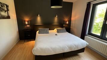 Quarto moderno com uma cama grande, duas luminárias de cabeceira, um painel de cabeceira escuro e uma janela com cortinas.