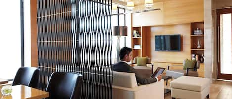 Um saguão de hotel moderno com área de estar, televisão e um painel preto decorativo.