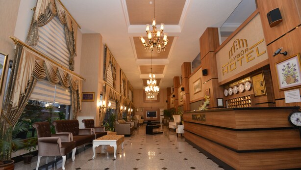 Um hall de hotel com balcão de recepção, área de estar, lustres e obras de arte.