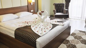 Cama bem arrumada com arranjo decorativo de toalhas, cabeceira de madeira e uma cadeira em quarto de hotel.