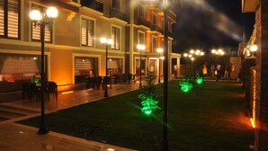 Vista noturna de um pátio de hotel com área de estar ao ar livre e entrada bem iluminada.