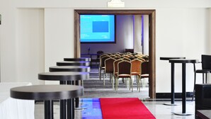 Uma sala de conferência com fileiras de cadeiras, uma tela de projetor e um tapete vermelho.