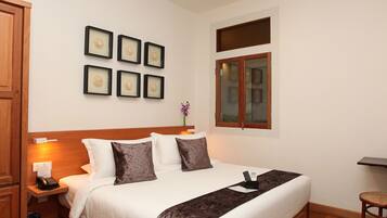 Cama bem arrumada com cabeceira de madeira, mesa de cabeceira com telefone e criado-mudo. Seis quadros emoldurados na parede acima da cama.
