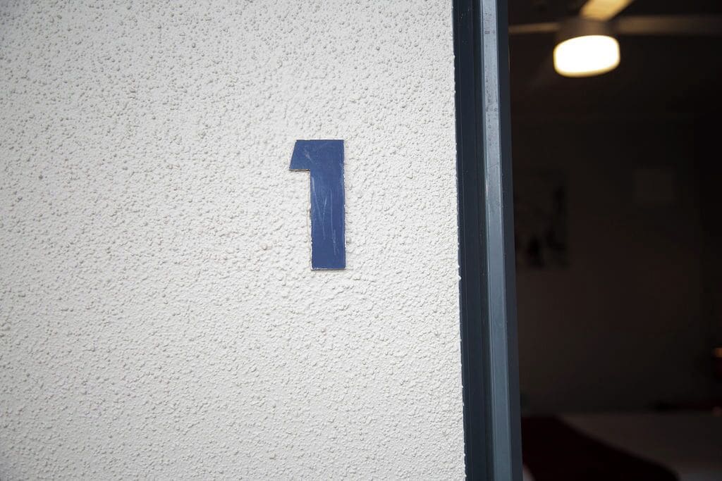 Parede branca com textura e um sinal azul com o número 1.