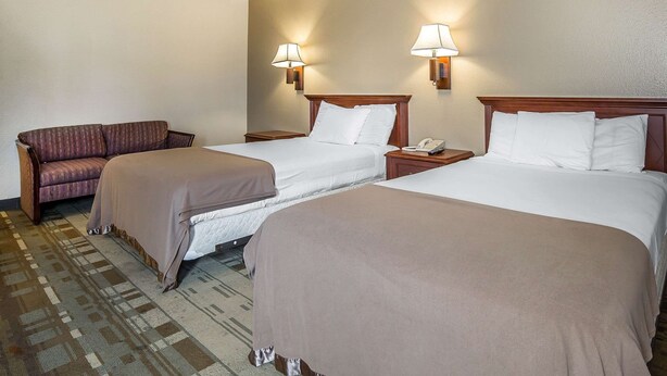 Quarto de hotel com duas camas, um sofá e duas luminárias fixadas na parede.