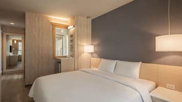 Quarto de hotel com uma cama grande, mesas de cabeceira, um espelho e uma luminária na parede.