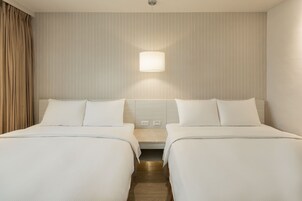 Quarto de hotel com duas camas, parede listrada em tom claro, luminária pendente e piso de madeira.