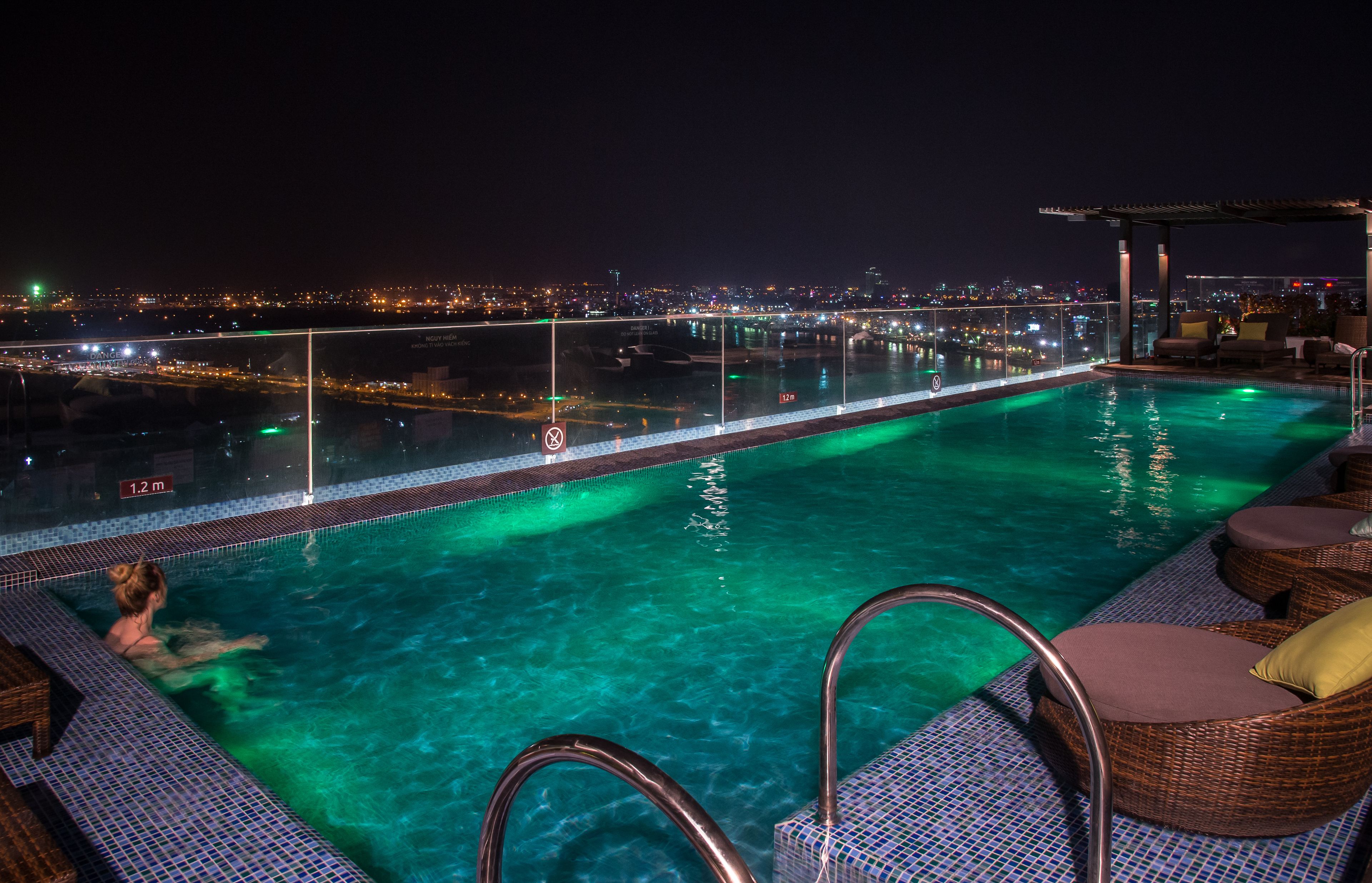 Piscina infinita no terraço com água cristalina, vista da cidade e espreguiçadeiras.