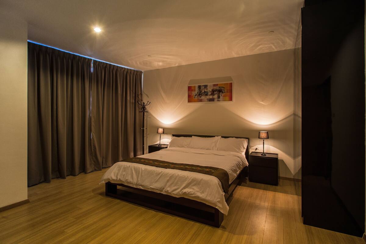 Um quarto moderno com uma cama grande, duas mesas de cabeceira, um porta-roupas e um quadro na parede.