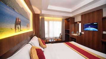 Quarto de hotel com uma cama grande, uma escrivaninha, uma cadeira, uma televisão e um quadro de uma paisagem pitoresca.