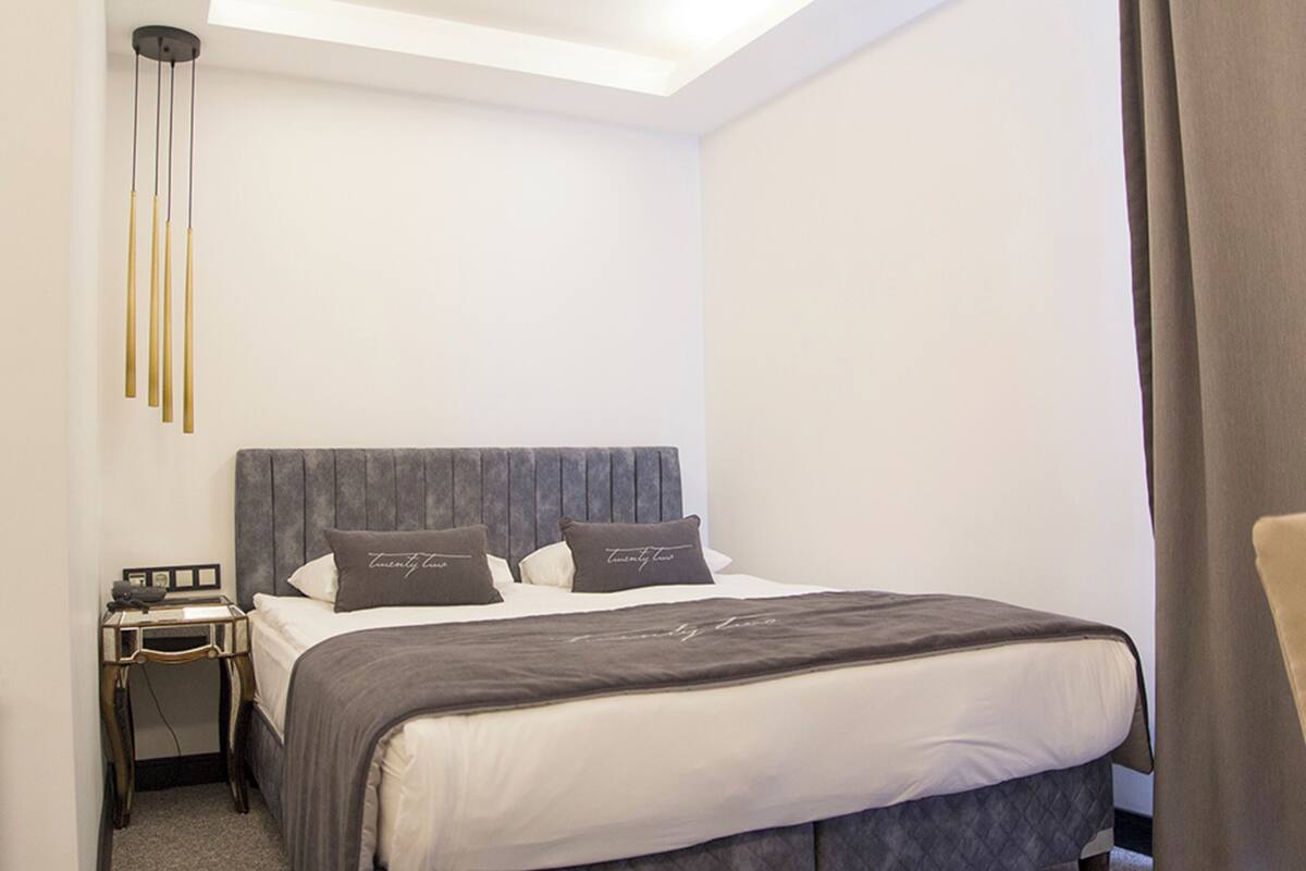 Quarto de hotel com cama, mesa de cabeceira e luminária suspensa.