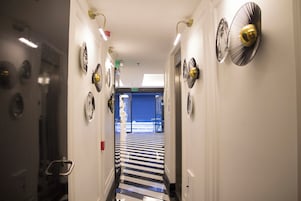 Um corredor com piso listrado, vários ventiladores fixados na parede e uma porta no final.