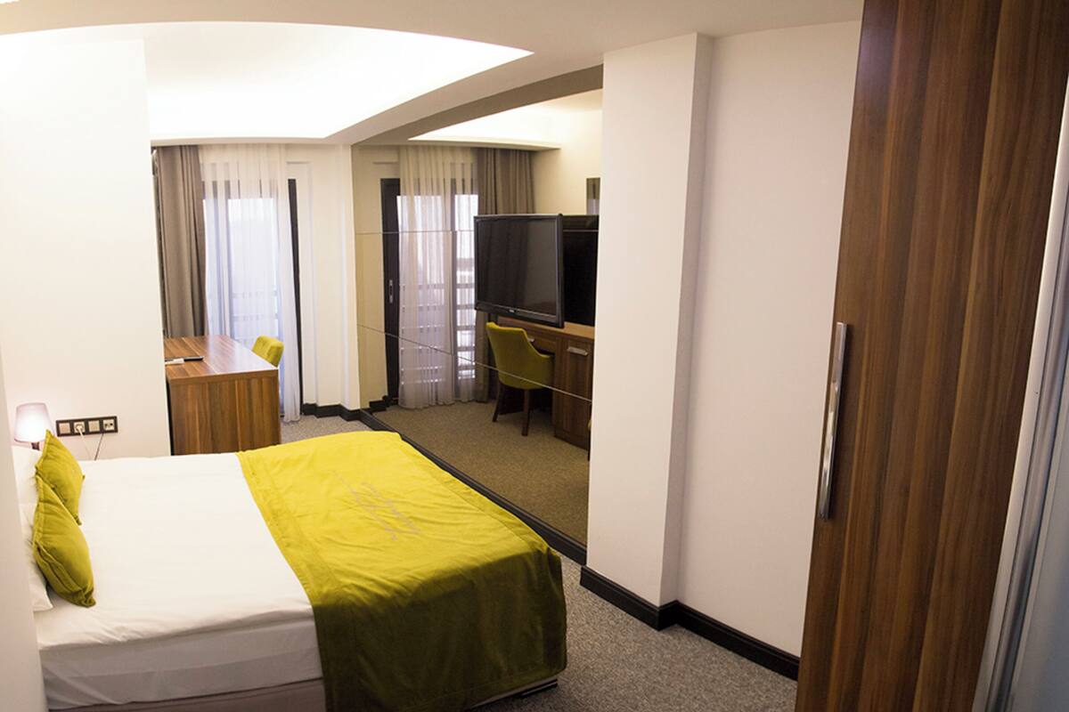 Quarto de hotel com cama, escrivaninha, cadeira, televisão e guarda-roupa.