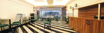 Um saguão de hotel com piso em preto e branco listrado, cadeiras estofadas em verde, um balcão de recepção de madeira e uma grande janela com vista para a cidade.