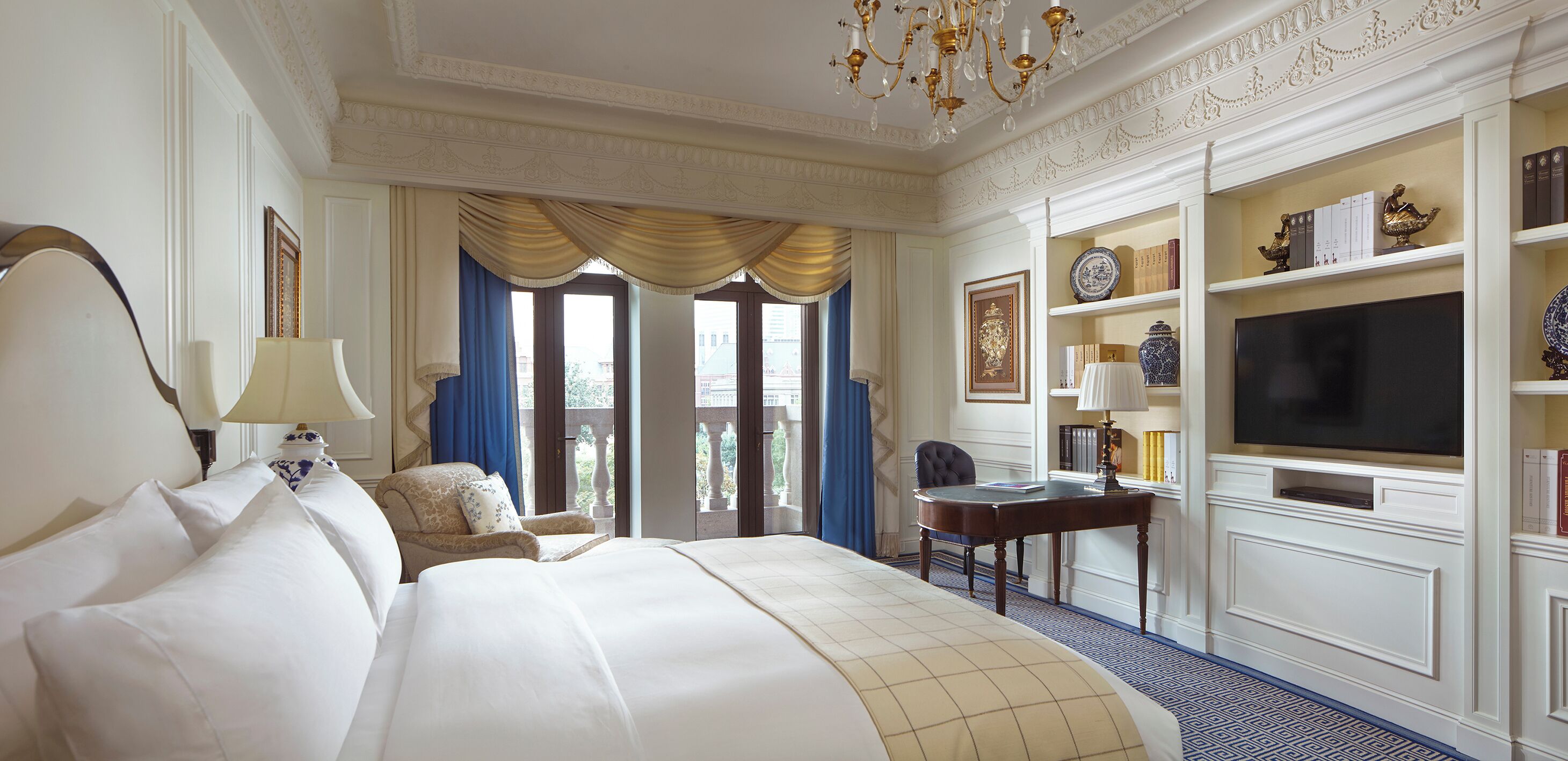 Quarto de hotel com uma cama grande, uma escrivaninha, uma televisão e uma estante de livros.