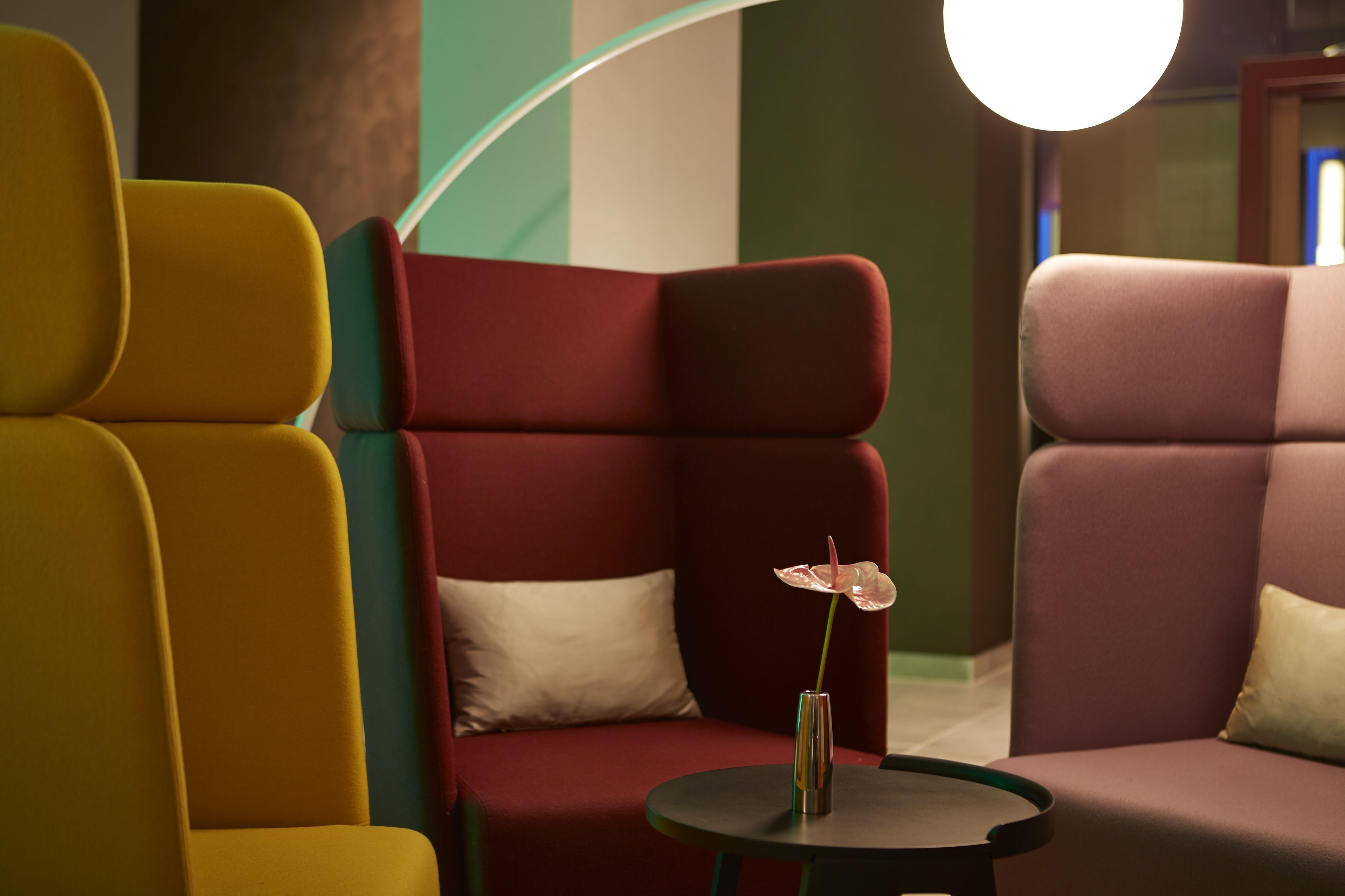Quarto moderno com uma cadeira vermelha e amarela, uma mesinha com um vaso e uma luminária curva singular.
