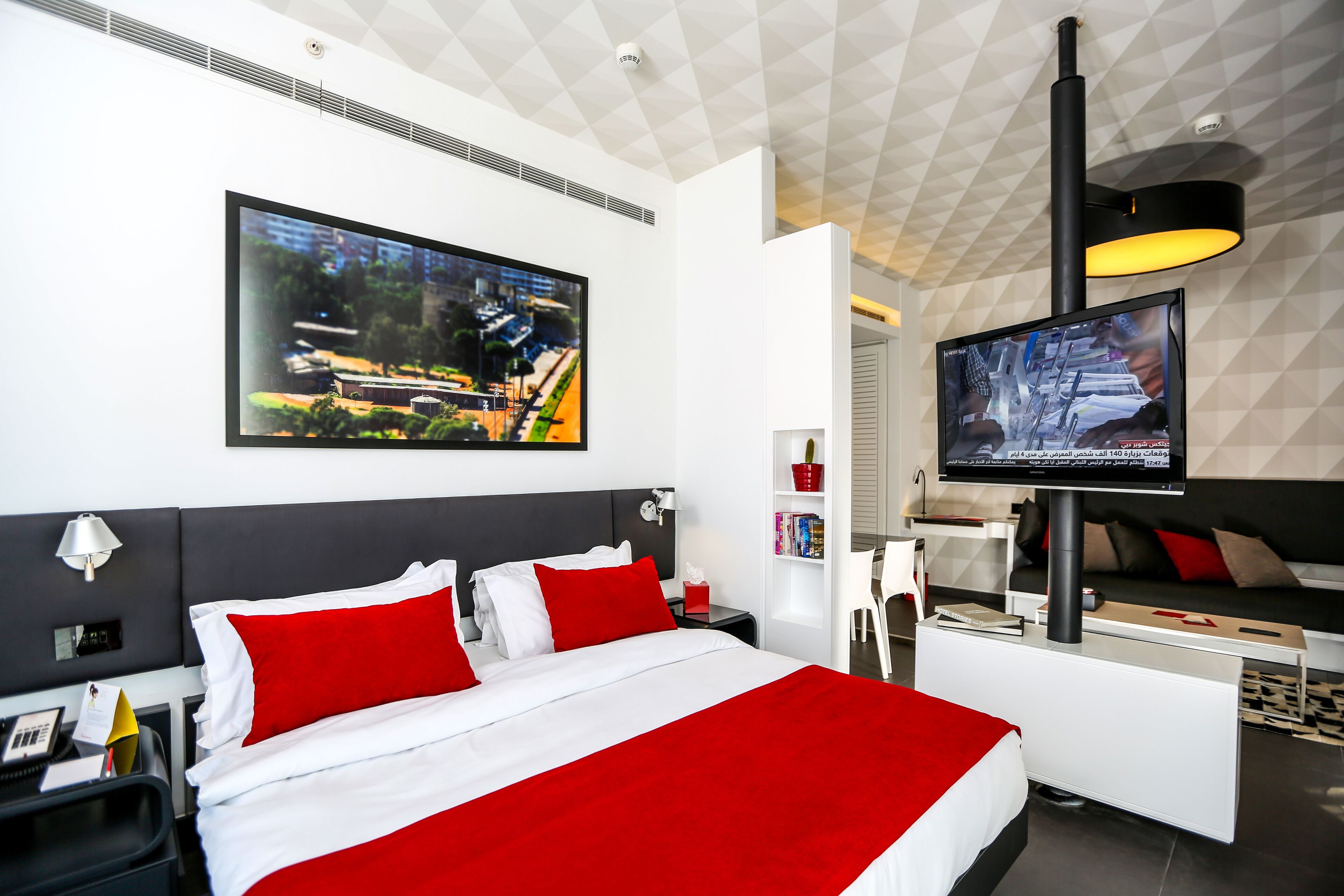 Quarto de hotel moderno com uma cama grande, televisão de tela plana, uma escrivaninha e uma estante de livros.