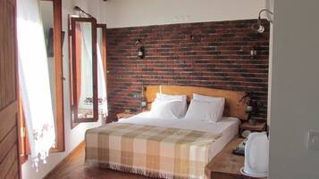 Quarto com teto de madeira, parede de tijolos, cama com manta xadrez, mesa de cabeceira e um pequeno frigorífico.
