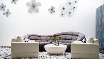 Uma sala de estar moderna com um sofá cinzento, duas poltronas, uma mesa de centro redonda com um vaso de flores e arte decorativa nas paredes.