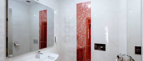 Casa de banho moderna com lavatório branco, espelho e chuveiro.