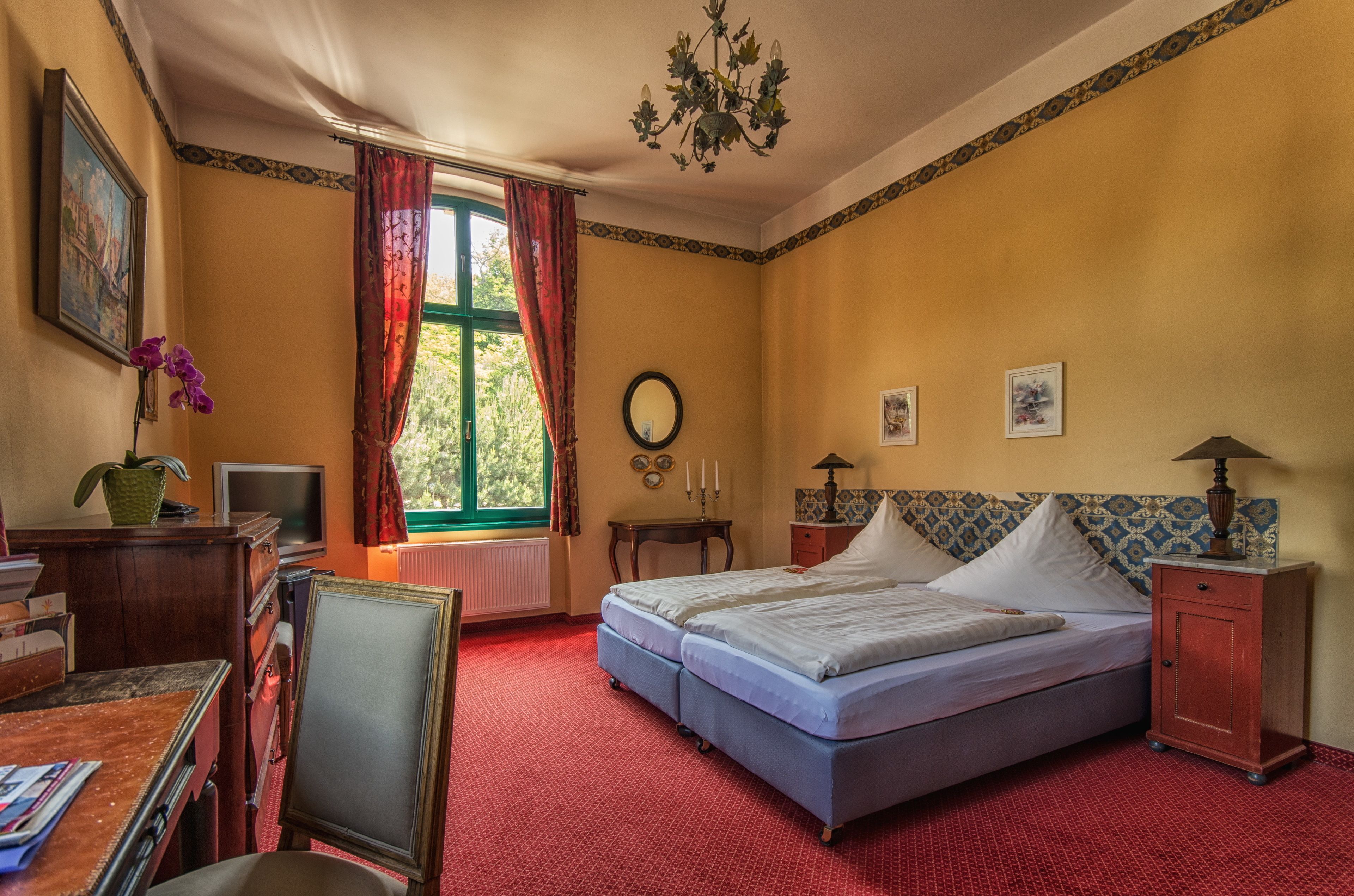 Um quarto com cama, escrivaninha, cadeira, cômoda e janela com cortinas.