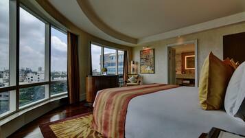 Quarto de hotel com uma cama grande, uma escrivaninha e vista da cidade através de amplas janelas.