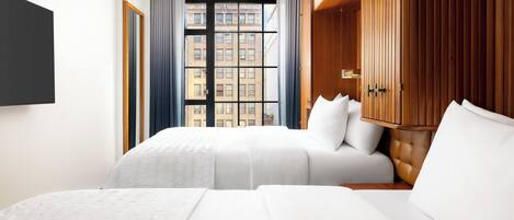 Quarto de hotel com duas camas, uma janela ampla com vista para a cidade, guarda-roupa de madeira e televisão de tela plana na parede.