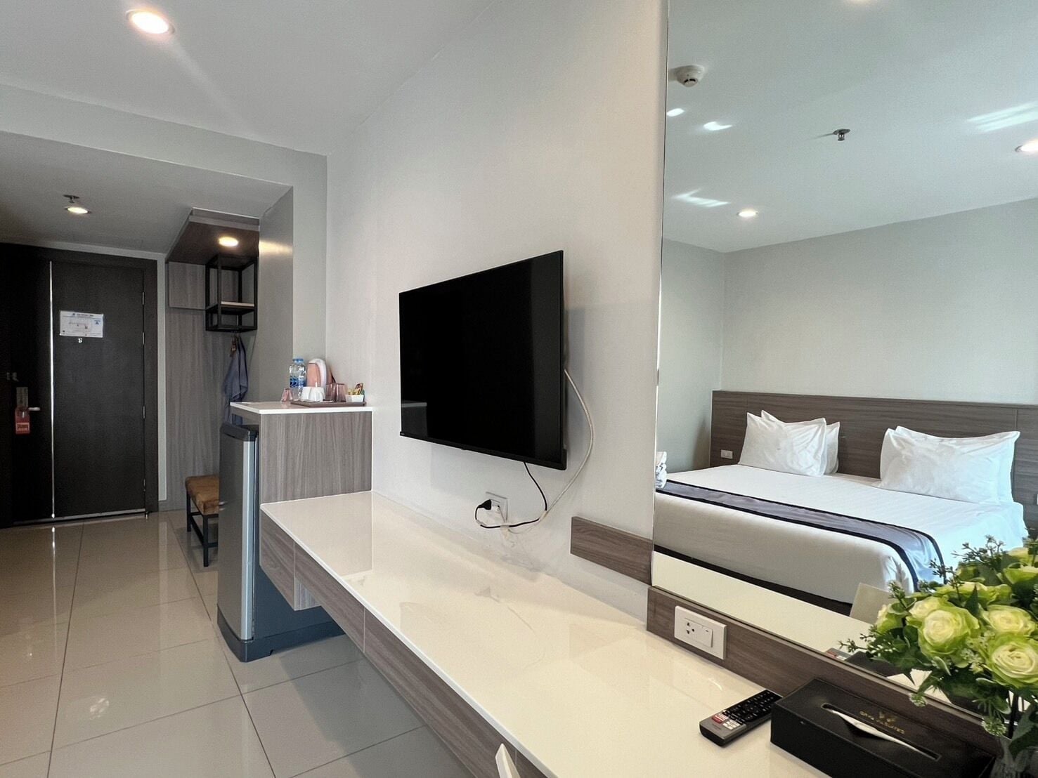 Quarto de hotel com uma cama, televisão fixada na parede, escrivaninha com cadeira e uma pequena mesa com artigos de higiene pessoal.