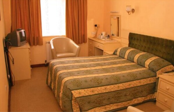 Quarto de hotel com uma cama, uma cadeira, uma escrivaninha e uma televisão.