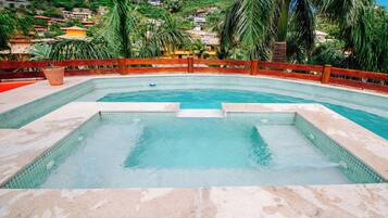Piscina retangular com borda azulejada, cercada por uma vedação de madeira e palmeiras ao fundo.