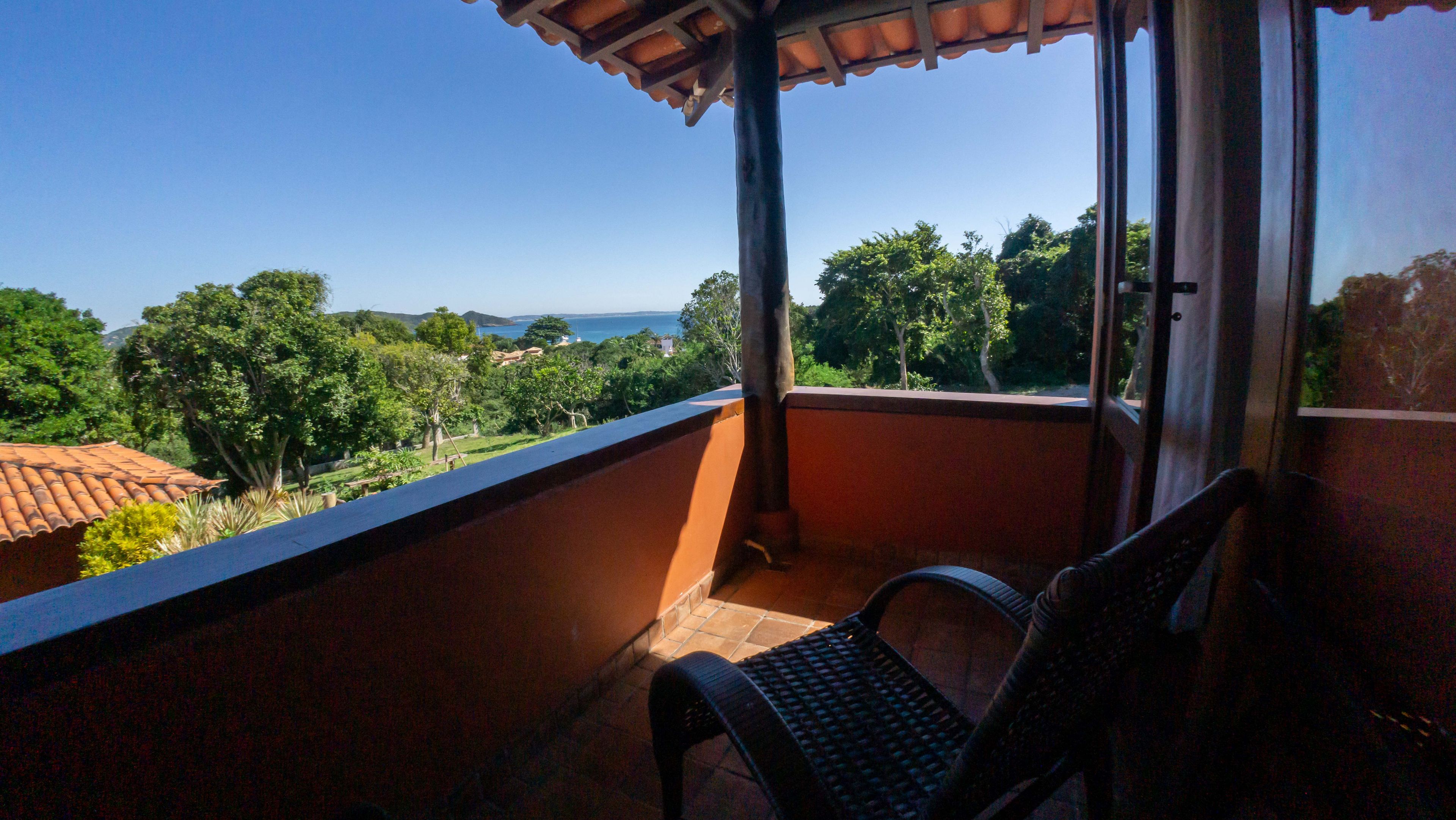 Varanda com vista para a paisagem costeira, uma cadeira e piso de azulejos.
