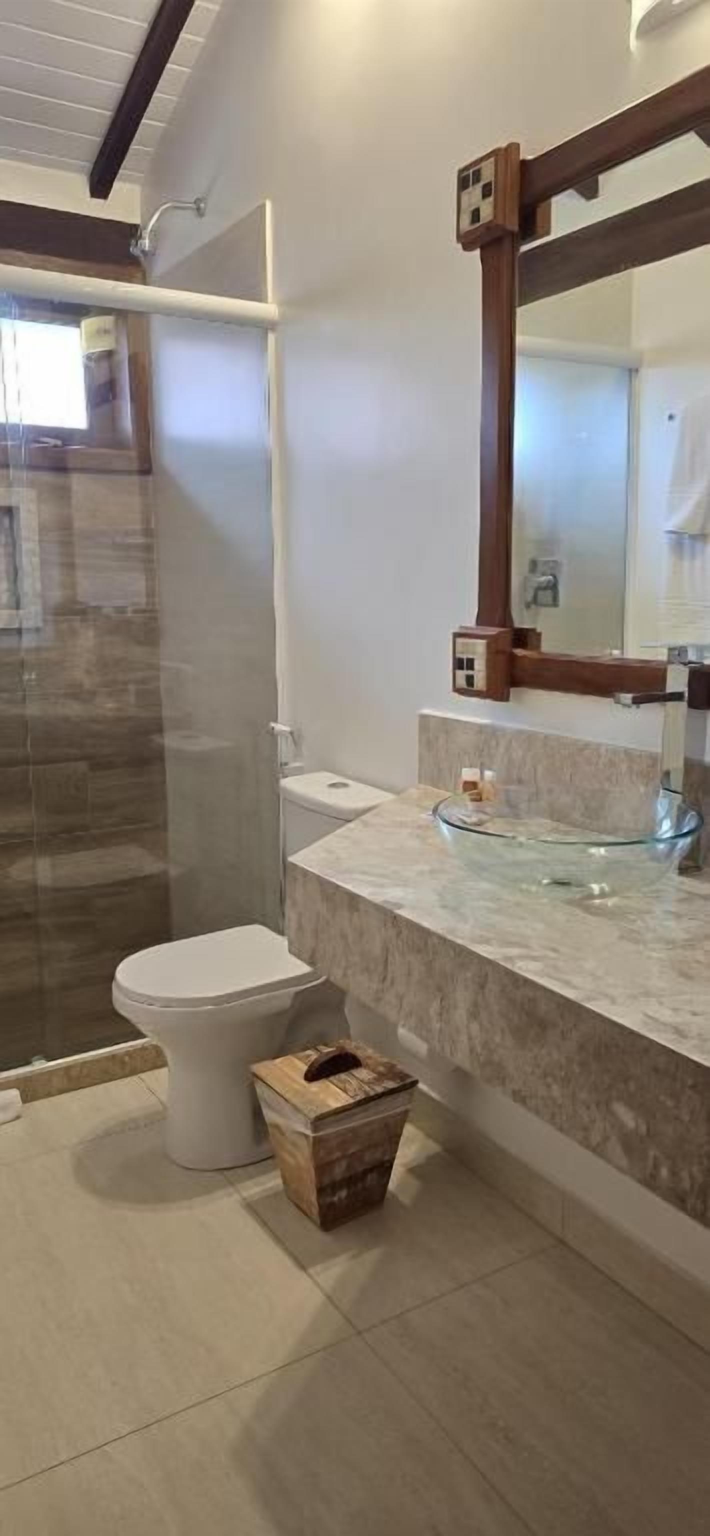 Casa de banho com cabine de duche em vidro, sanita, lavatório de mármore e espelho com moldura de madeira.