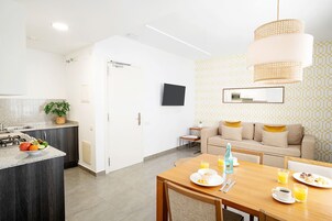 Cozinha moderna com área de refeições, sofá e TV fixada na parede.