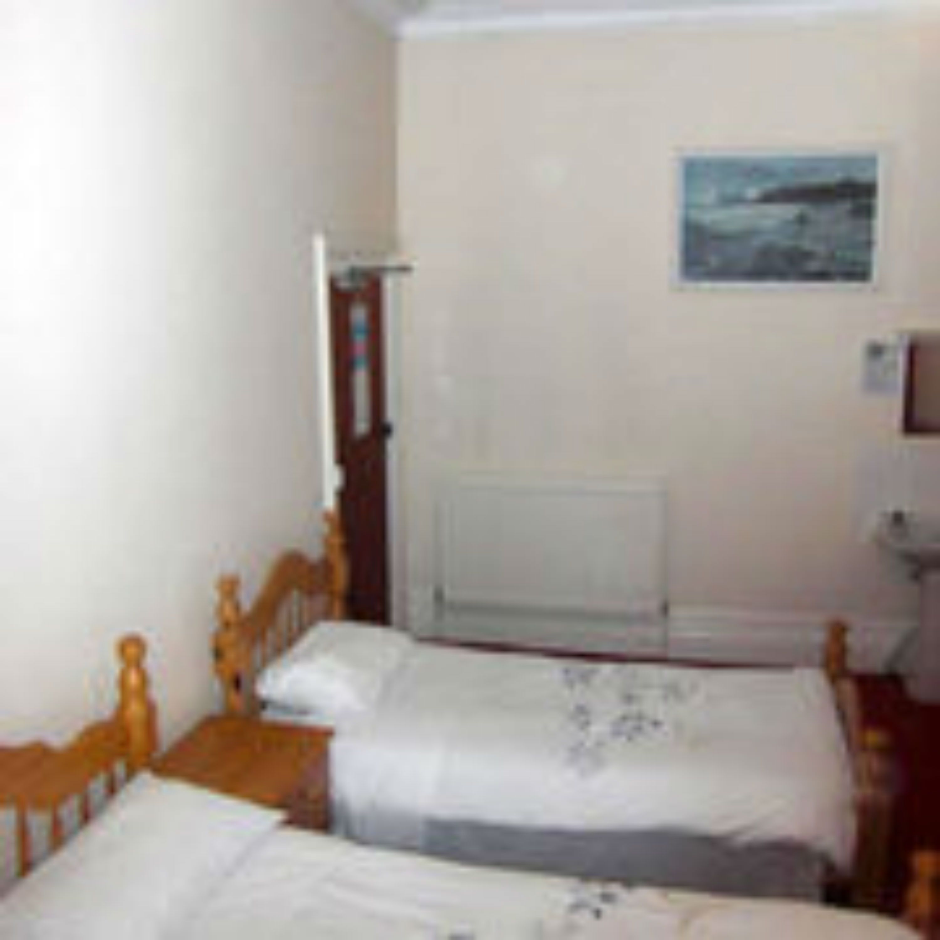 Quarto com duas camas de solteiro, cabeceira de madeira, radiador e um quadro na parede.