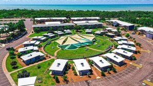 Um resort com diversas acomodações em estilo de bangalô dispostas em torno de uma área central ajardinada, um estacionamento e vista para o oceano.