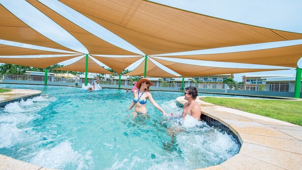 Piscina com várias pessoas, protegida por grandes toldos.