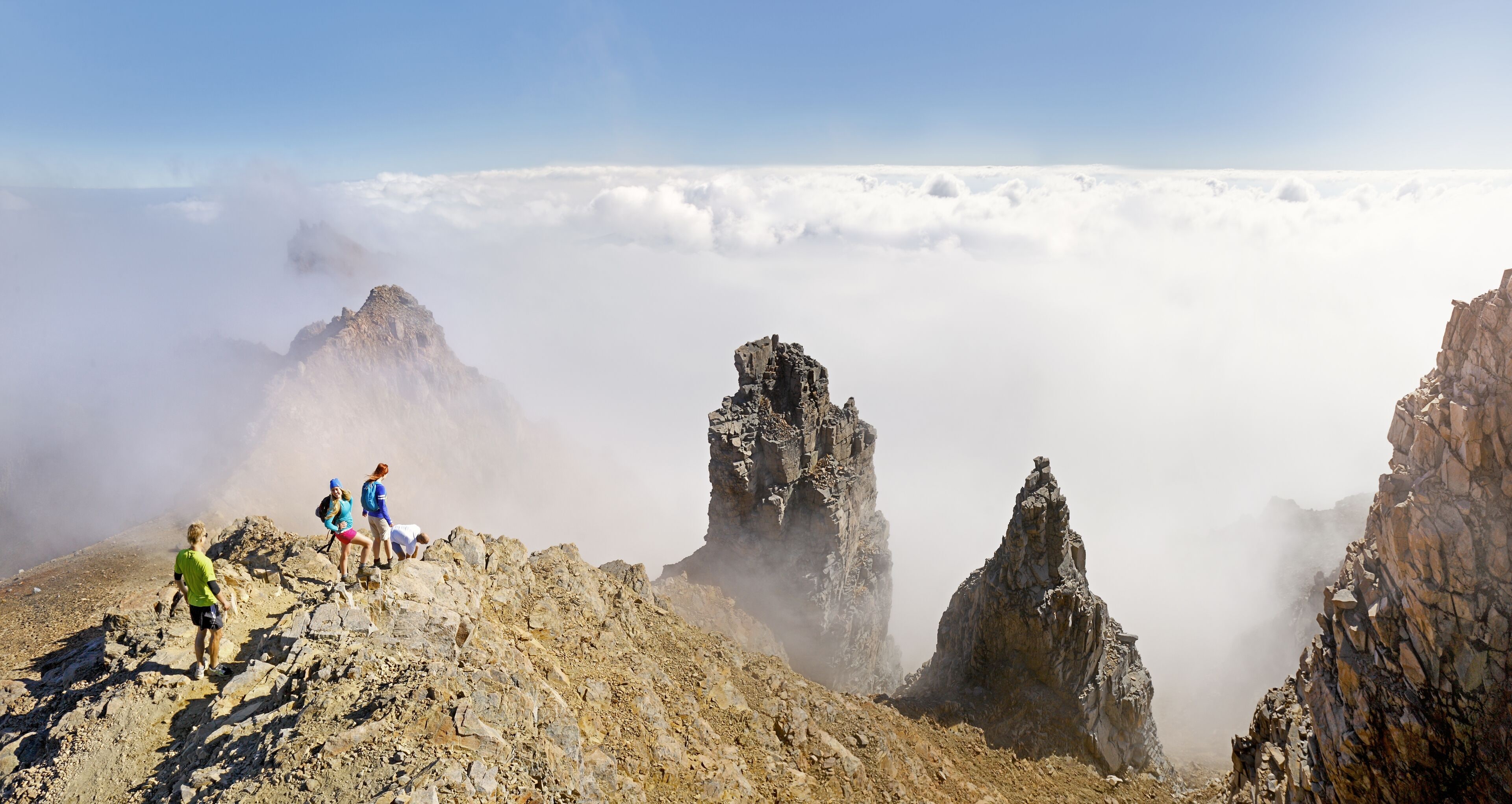 Um pico montanhoso rochoso com caminhantes no cume.