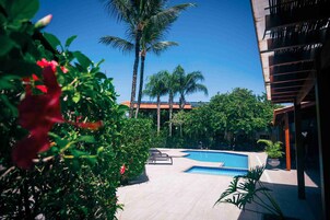 Uma piscina rodeada por palmeiras e vegetação, com um edifício ao fundo.