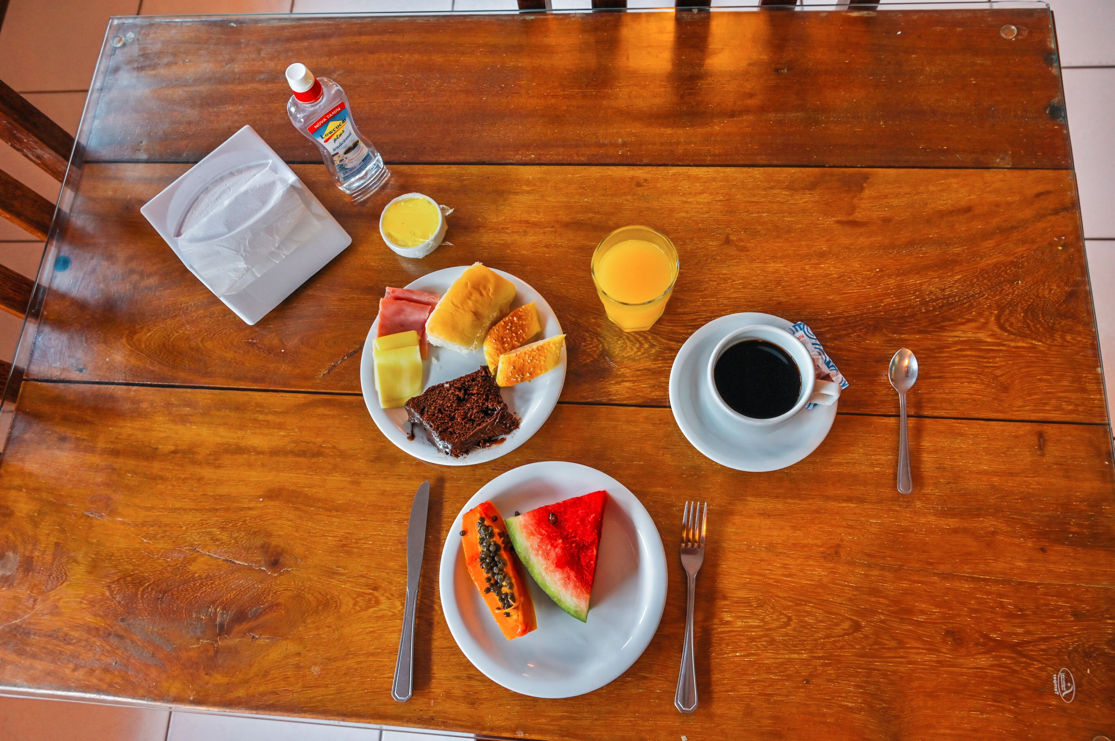 Uma mesa de madeira com pratos de comida, uma garrafa de detergente, um copo de suco e uma xícara de café.